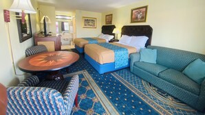 Quarto de hotel com duas camas, um sofá, uma mesa redonda e um tapete estampado.
