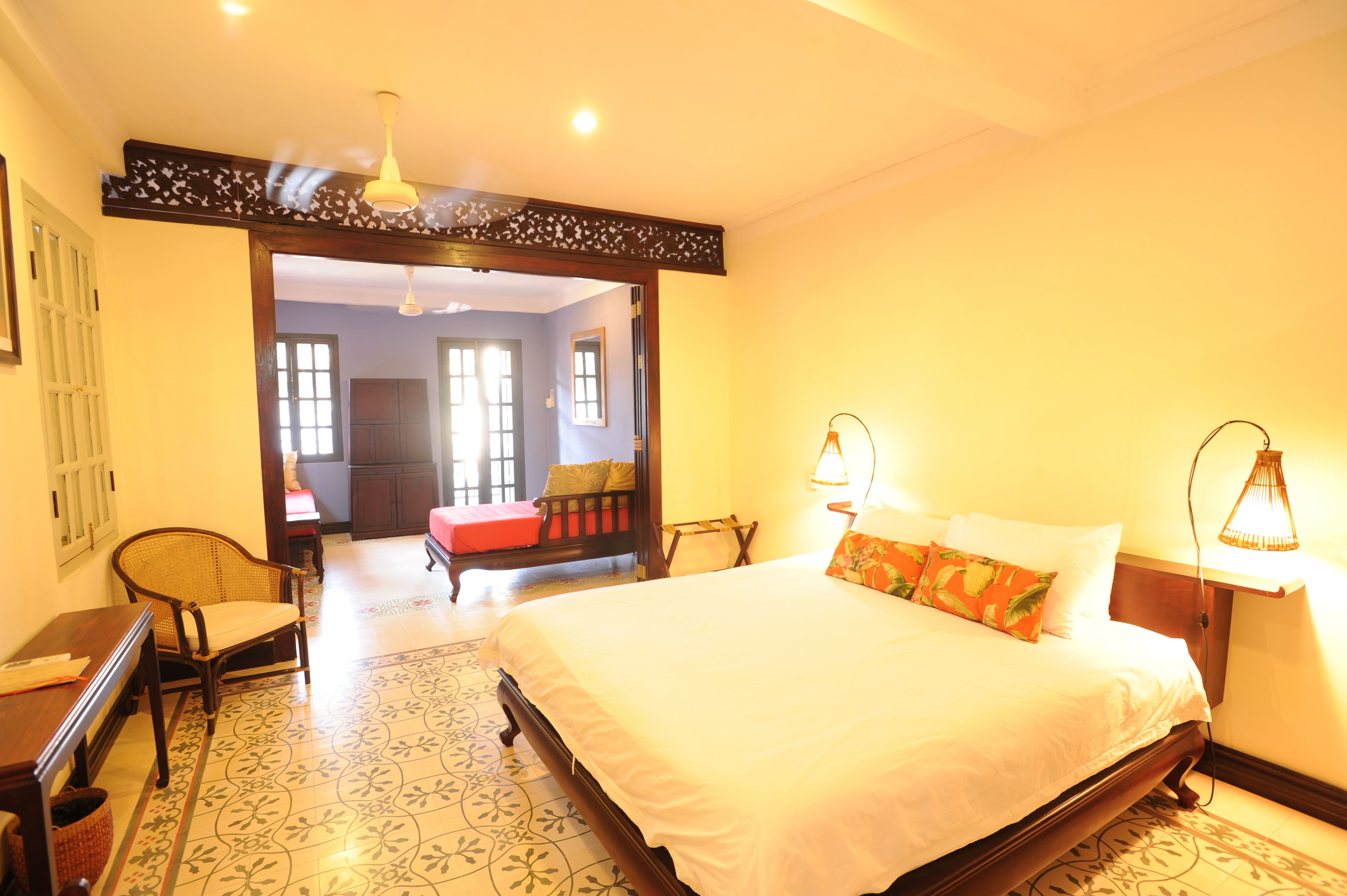 Quarto de hotel com uma cama grande, uma cadeira de madeira, uma escrivaninha e um chão estampado.
