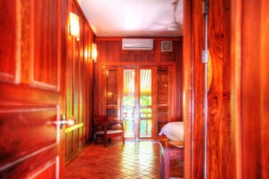 Um corredor de madeira com uma cama, uma cadeira e um ventilador de teto.