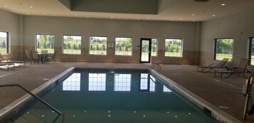 Uma grande piscina coberta com paredes de vidro transparente, várias janelas e uma porta identificada por uma placa de saída.