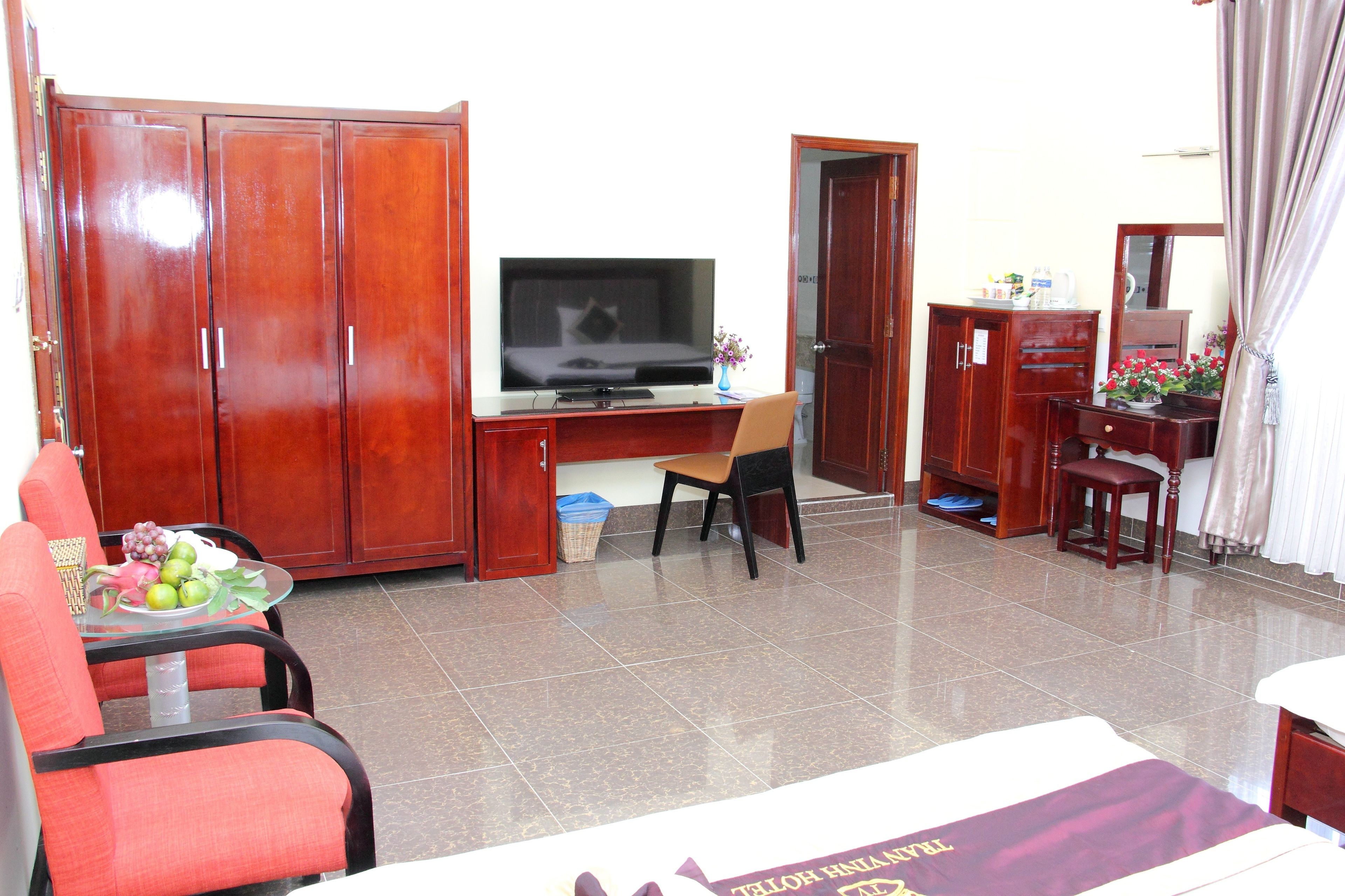 Quarto de hotel com cama, televisão, secretária com cadeira, guarda-roupa e uma pequena mesa com fruta.