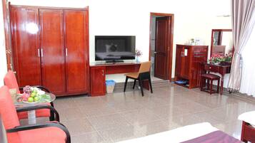 Quarto de hotel com cama, televisão, secretária com cadeira, guarda-roupa e uma pequena mesa com fruta.