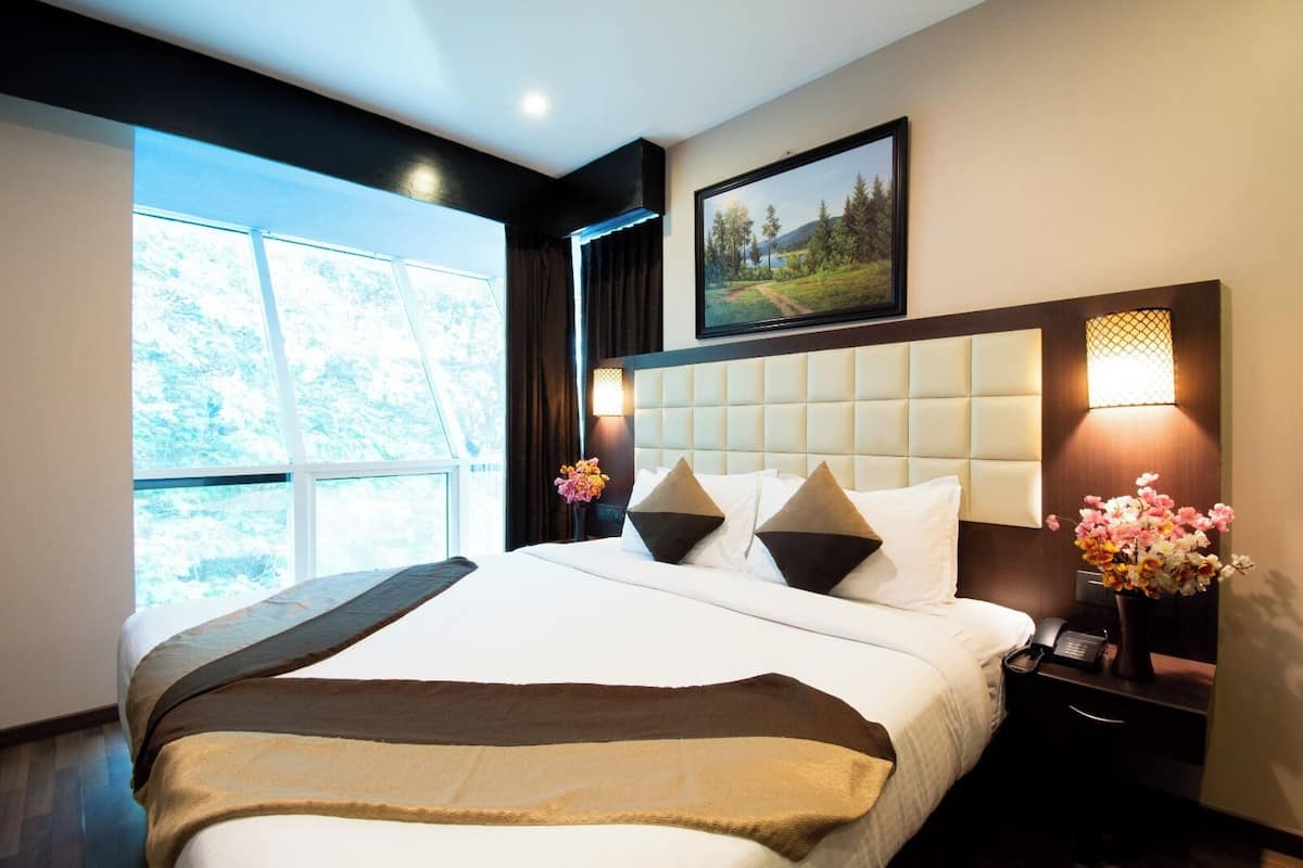 Quarto de hotel com uma cama grande, janela com vista, um quadro na parede e mesa de cabeceira com abajur e telefone.