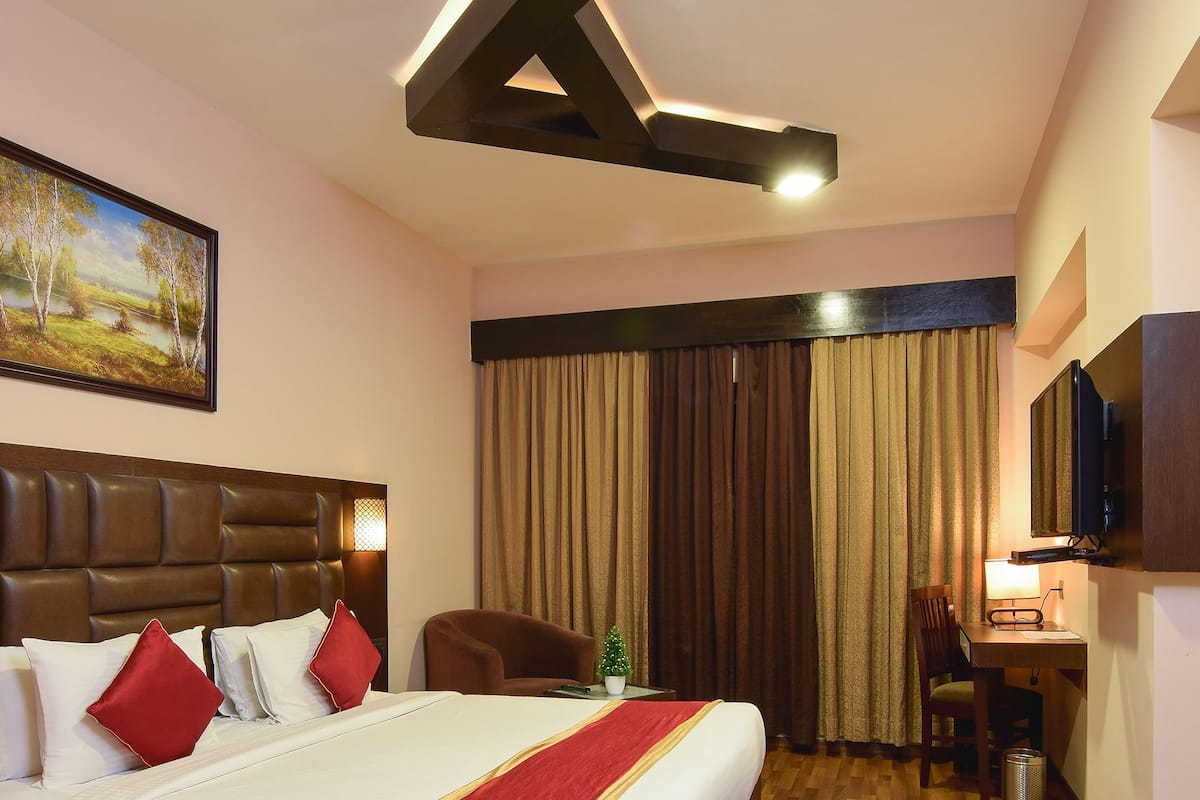 Quarto de hotel com uma cama grande, uma escrivaninha, uma cadeira, uma televisão e uma janela com cortinas.
