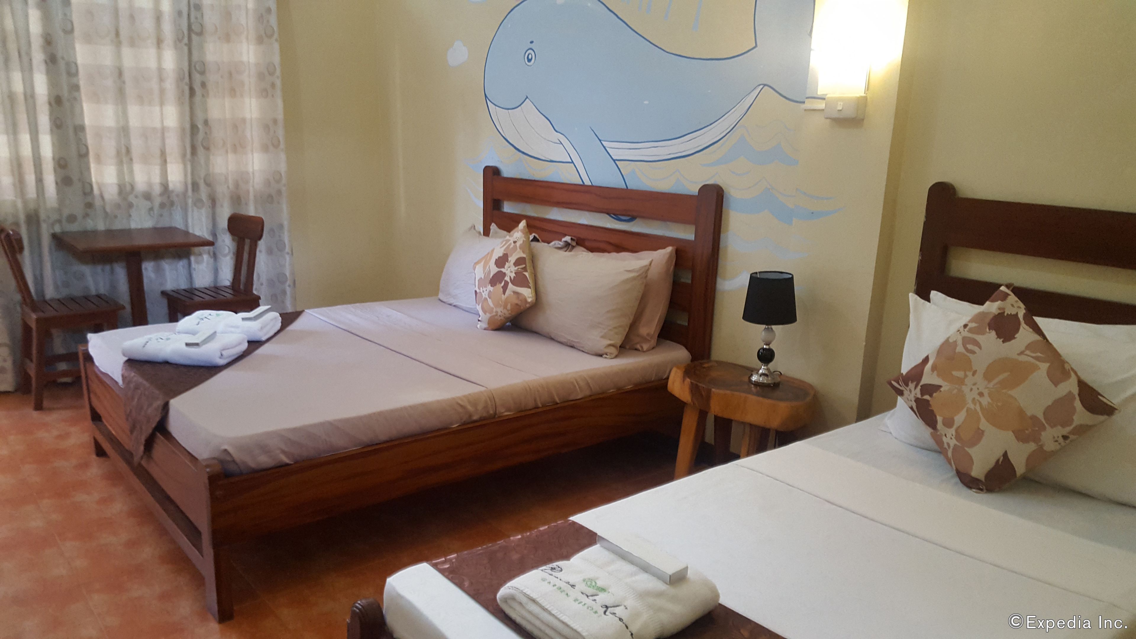 Quarto com cama de madeira, mesa de cabeceira pequena com luminária, uma cadeira e um mural decorativo na parede.