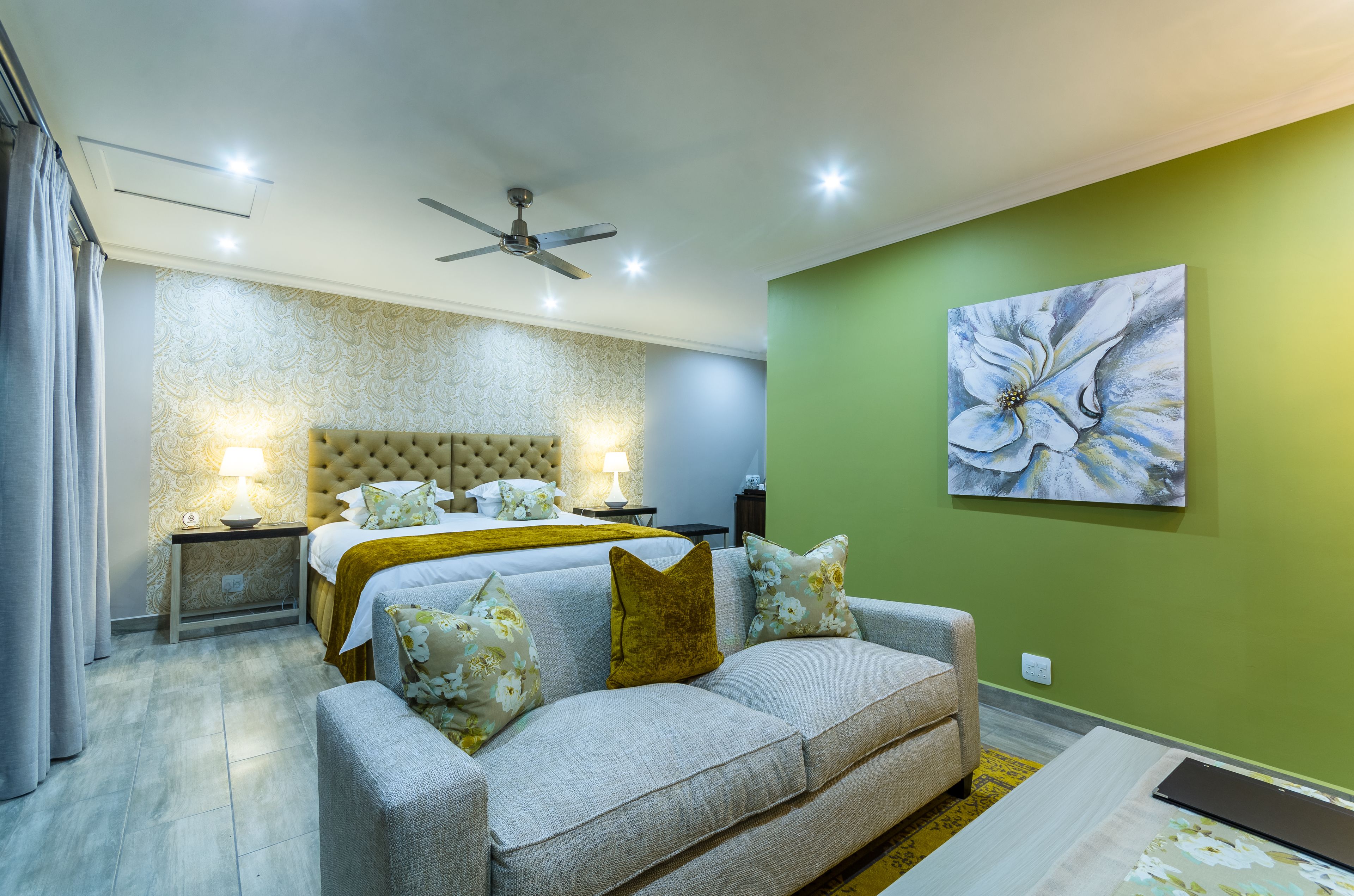 Quarto moderno com cama, sofá, ventoinha no teto e um quadro na parede.