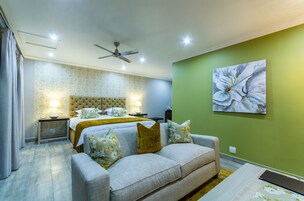 Quarto moderno com cama, sofá, ventoinha no teto e um quadro na parede.