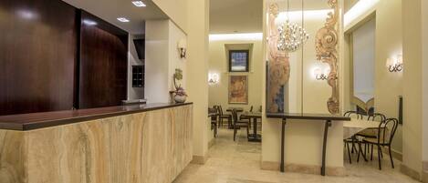 Uma área de recepção de hotel com um balcão de mármore, uma sala de jantar com cadeiras e mesas, e um lustre.