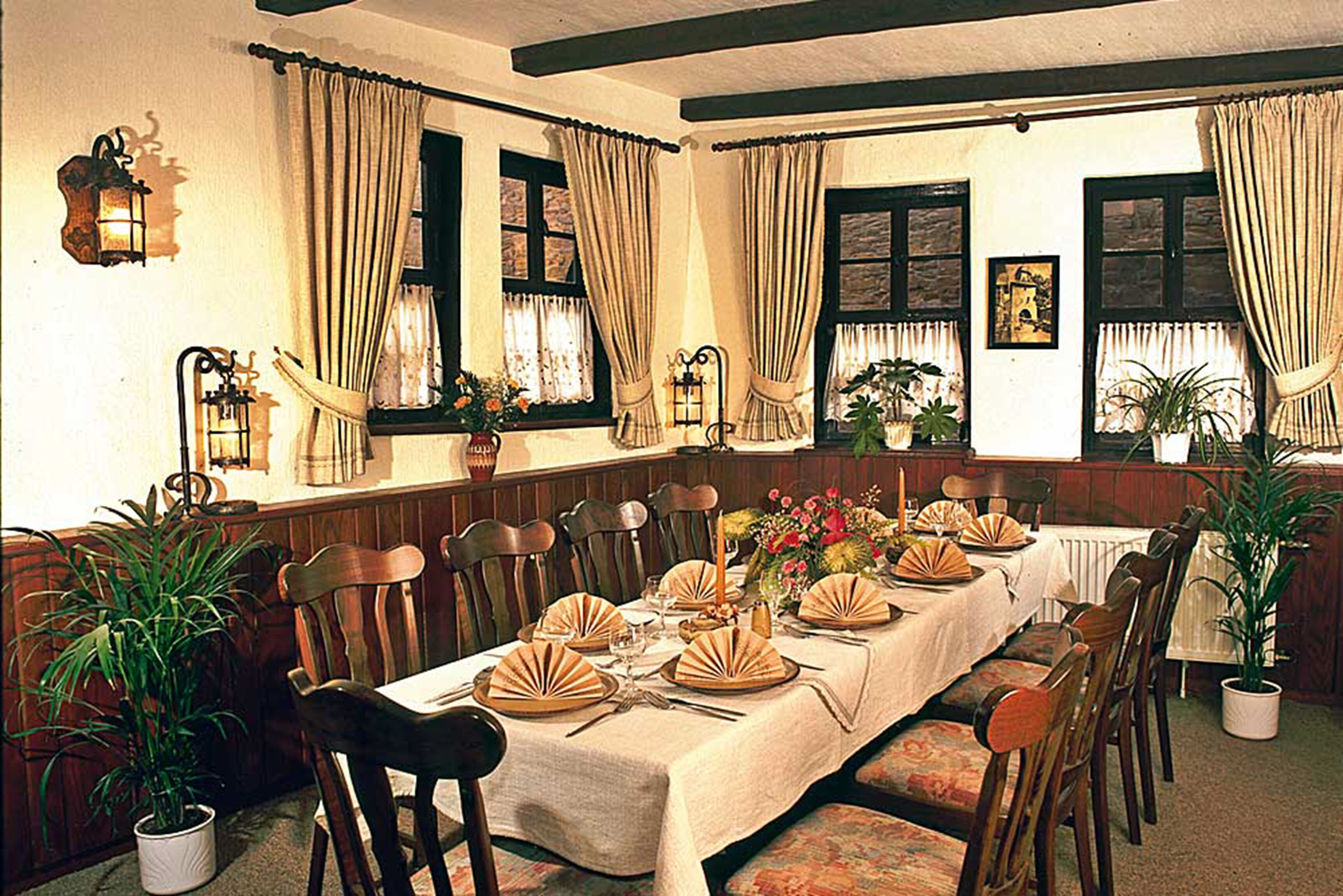 Uma sala de jantar com uma mesa comprida posta para refeição, rodeada por cadeiras de madeira.