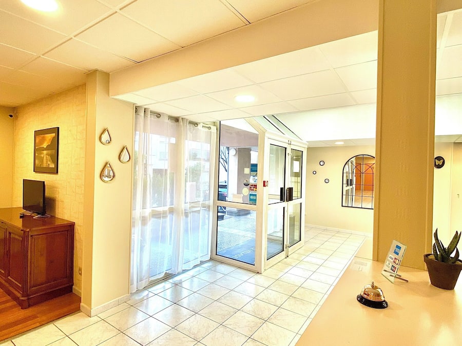 Um saguão de hotel com uma mesa de recepção, um armário de madeira, um vaso de planta e uma porta de vidro que dá para a entrada.