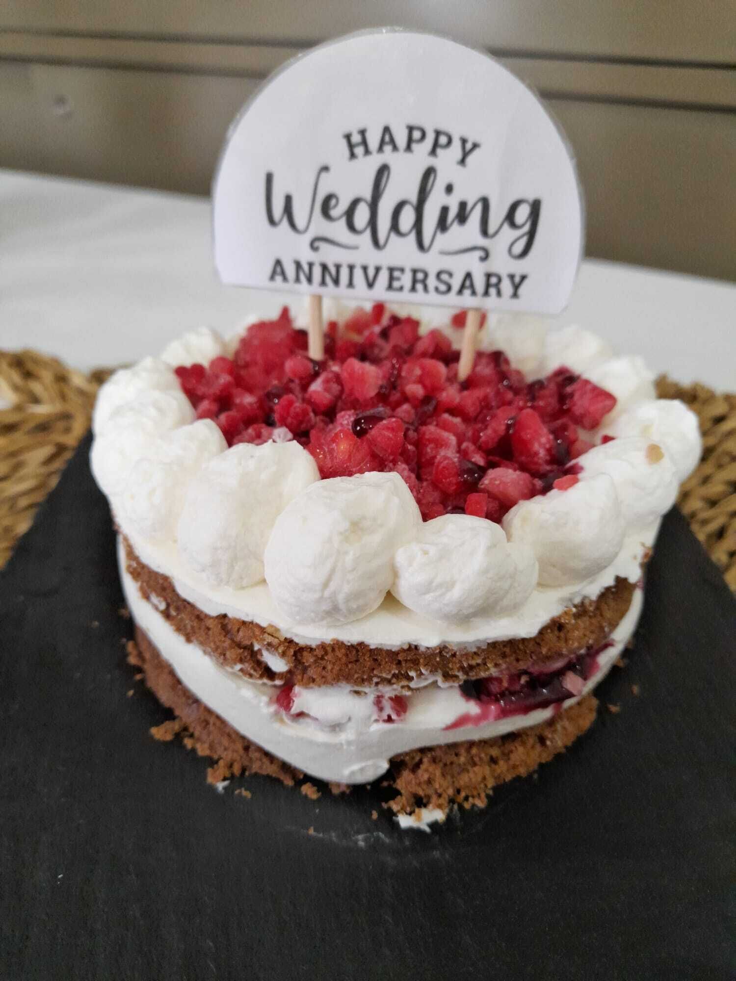 Um bolo de aniversário de casamento com um enfeite que diz 'Feliz Aniversário de Casamento'.