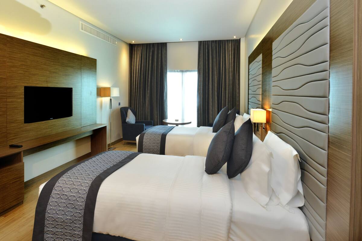 Quarto de hotel com uma cama grande, televisão, escrivaninha e vista para a cidade.