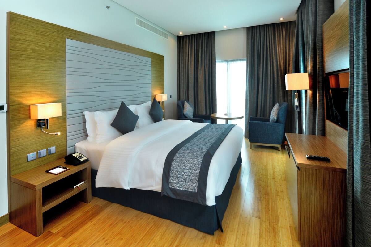 Quarto de hotel com uma cama grande, mesas de cabeceira, uma escrivaninha e uma televisão.