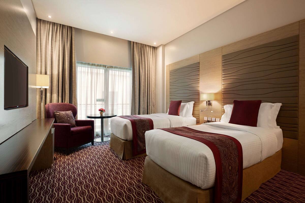 Quarto de hotel com duas camas, uma escrivaninha, televisão e vista para o exterior.