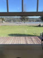 Vista de um quarto com uma janela grande para uma área gramada, um deck de madeira e uma estrada com um veículo.