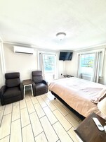 Quarto de hotel com cama, duas poltronas, uma mesinha, televisão e aparelho de ar condicionado.