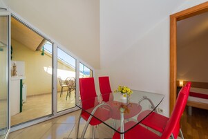 Uma sala de jantar moderna com mesa de vidro e cadeiras vermelhas, um vaso com flores amarelas e vista para um pátio externo.