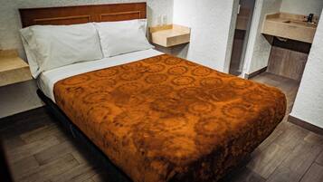 Cama bem arrumada com colcha estampada, cabeceira de madeira e mesa de cabeceira com abajur.