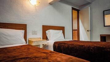 Quarto de hotel com duas camas, uma mesa de cabeceira, uma luminária na parede e uma porta que dá para outro cômodo.