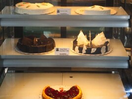 Uma vitrine com vários bolos, incluindo um bolo de chocolate e uma tarte de fruta.