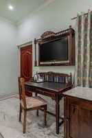 Uma sala de jantar com uma mesa de madeira, cadeiras, uma televisão presa à parede e uma cortina estampada.