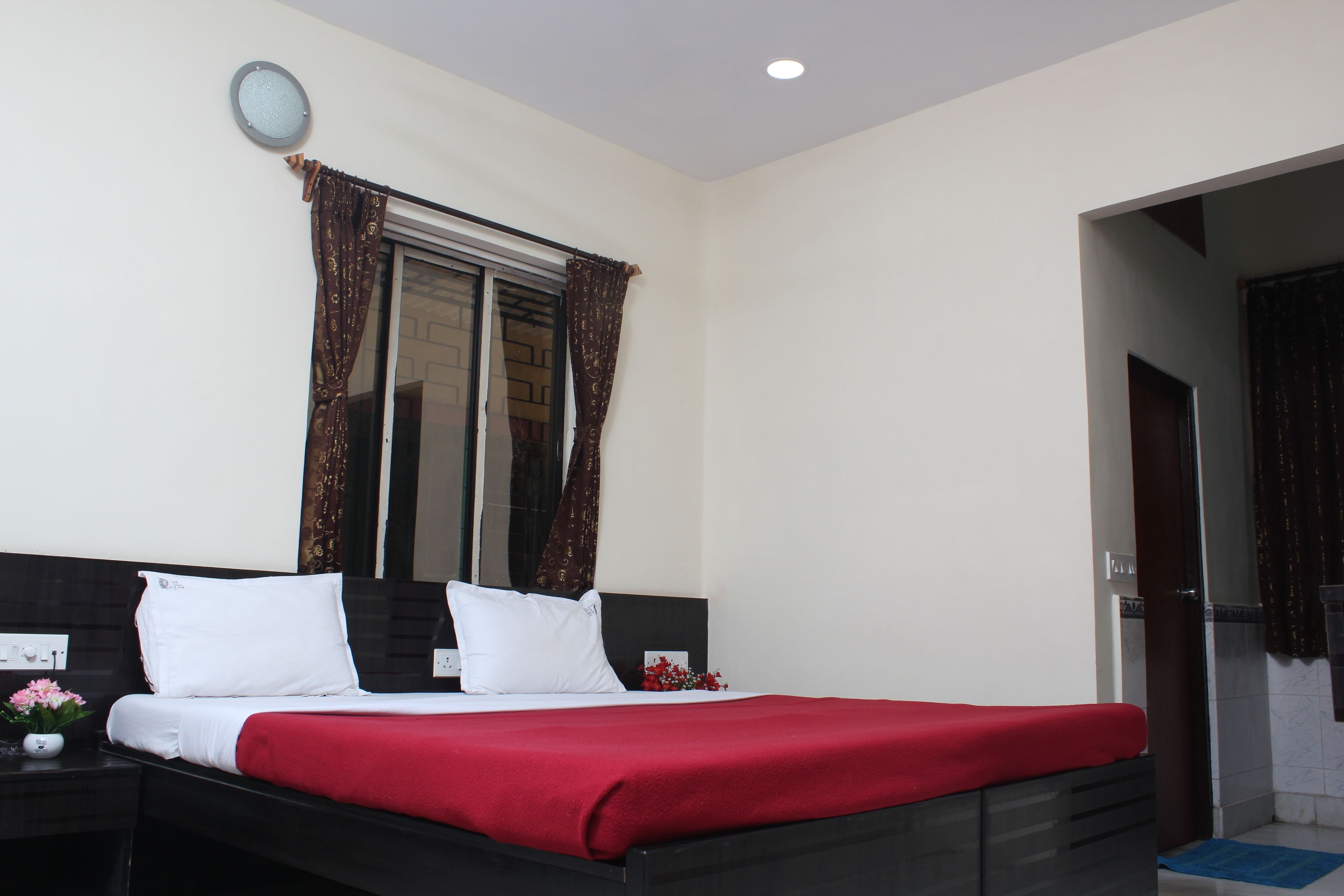 Quarto de hotel com cama, mesa de cabeceira, janela com cortinas e porta para um banheiro.