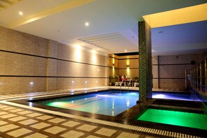 Piscina com piso ladrilhado e área de hidromassagem separada, ambos com iluminação.