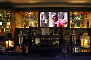 Um espaço de bar com uma tela de televisão, diversos frascos e um candeeiro decorativo.