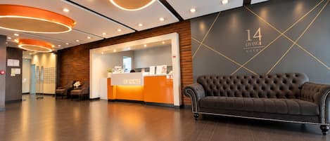 Um hall de recepção de hotel com design moderno, apresentando um balcão de atendimento, área de estar e um amplo sofá.