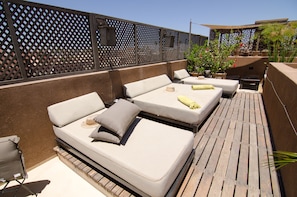 Terraço no telhado com dois sofás e uma mesa, rodeado por um deck de madeira e um cercado de treliça.