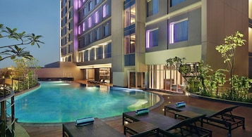 Um hotel moderno com piscina, áreas de descanso e fachada bem iluminada.