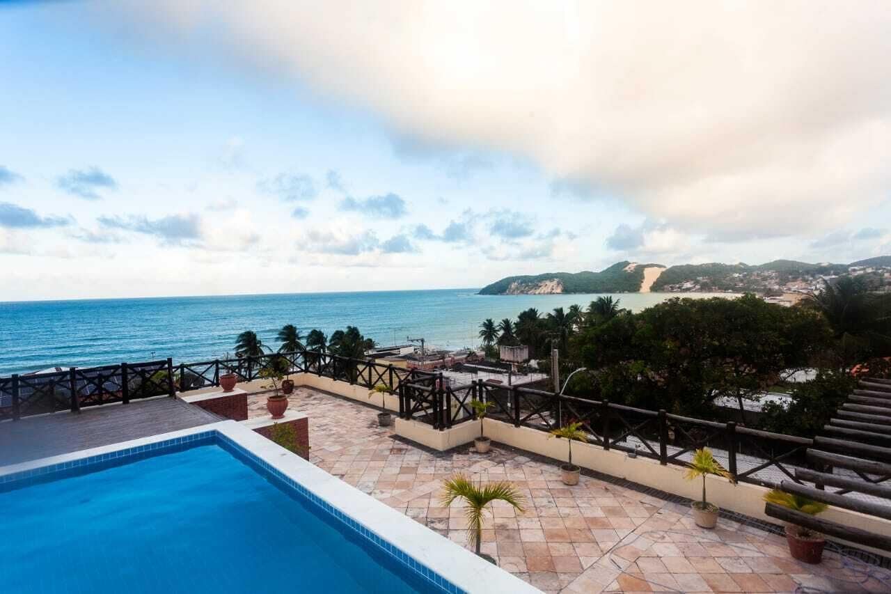 Piscina no terraço com vista para o oceano e uma cidade ao longe.