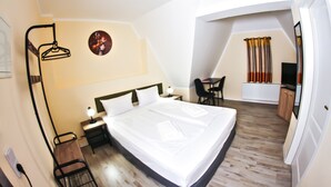 Quarto de hotel com uma cama grande, uma escrivaninha, uma cadeira, uma televisão e um relógio na parede.
