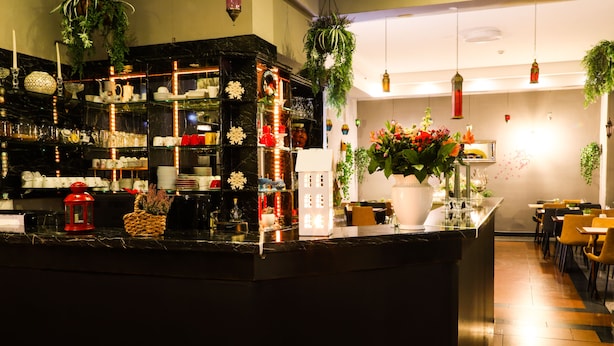 Uma área de bar com bancada de mármore, prateleiras com copos e um vaso branco com flores.