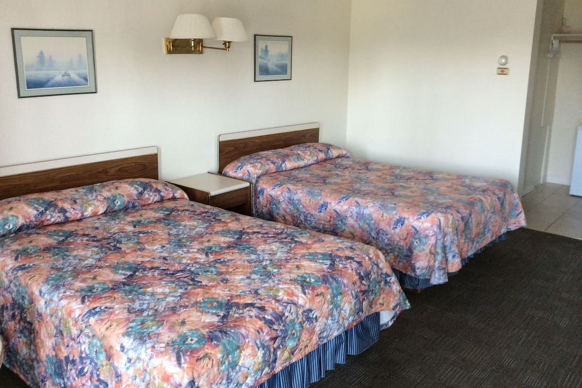 Quarto de hotel com duas camas, cada uma com colcha florida, mesa de cabeceira, luminária na parede e dois quadros emoldurados.