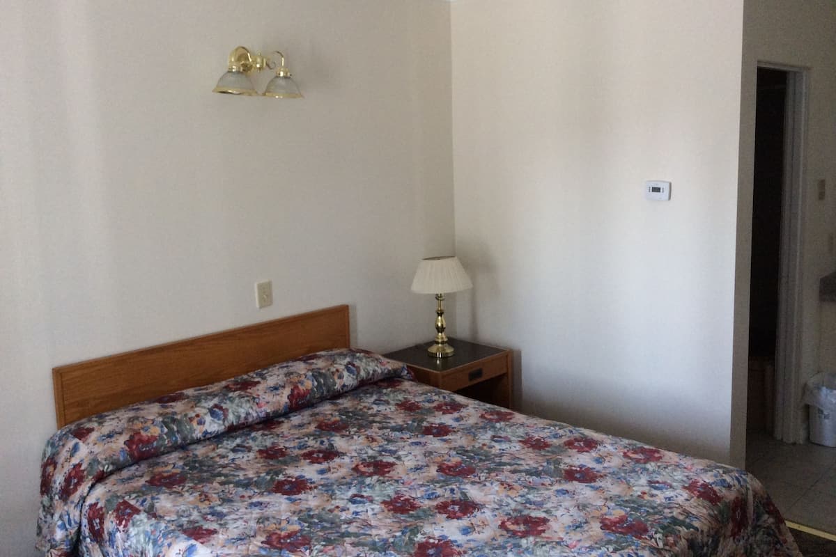 Quarto com cabeceira de madeira, colcha floral, luminária de mesa e luminária na parede.