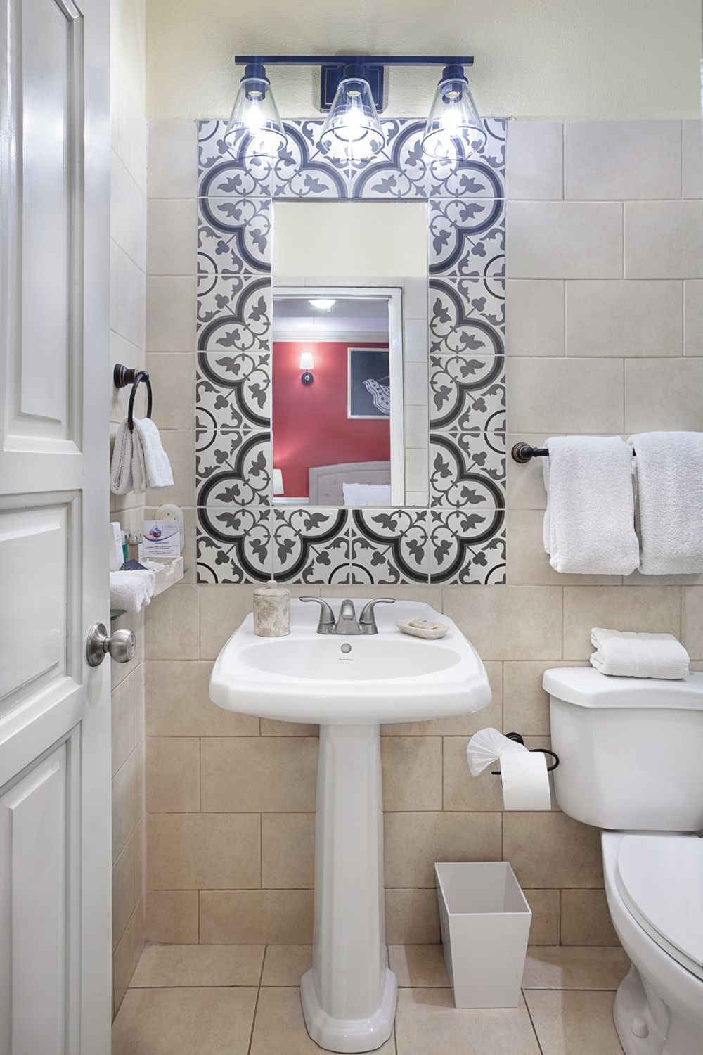 Casa de banho com lavatório assentado, sanita, lixeira e espelho com azulejos decorativos.