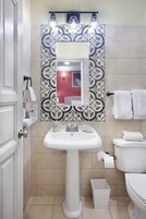 Casa de banho com lavatório assentado, sanita, lixeira e espelho com azulejos decorativos.