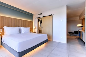 Quarto de hotel moderno com uma cama grande, mesas de cabeceira, escrivaninha e guarda-roupa.