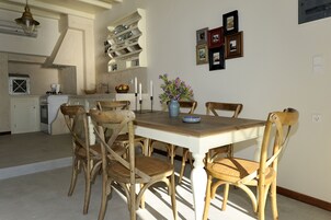 Uma sala de jantar com uma mesa e cadeiras de madeira, um vaso com flores e uma cozinha ao fundo.