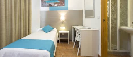 Quarto de hotel com cama, escrivaninha, cadeira, banheiro com chuveiro e um quadro na parede.