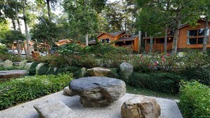 Resort com cabanas de madeira, cercado por um jardim ajardinado com pedras grandes e vegetação densa.