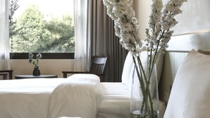 Quarto de hotel com uma cama, uma mesinha com um vaso de flores e vista para árvores pela janela.