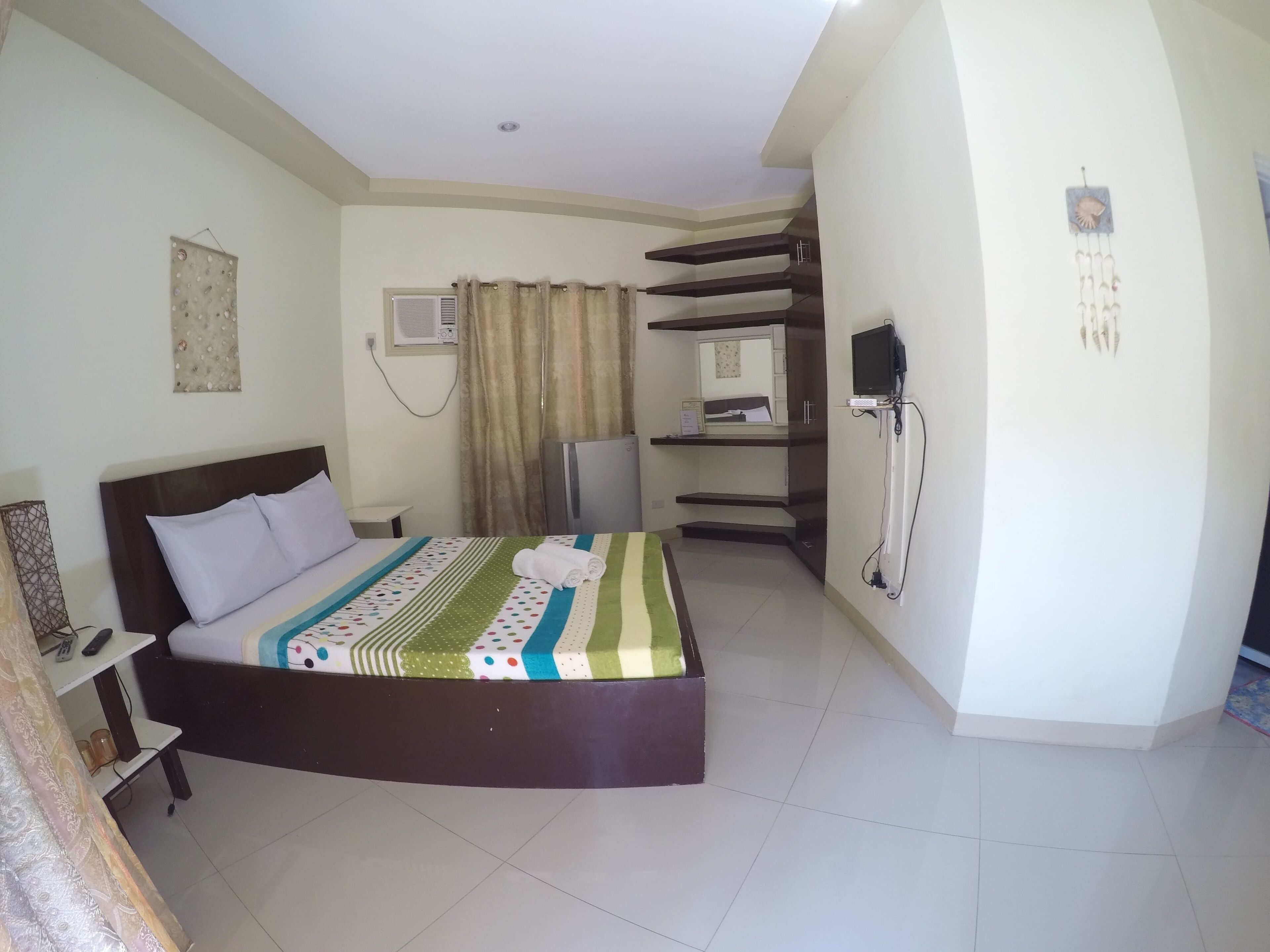 Um quarto com cama, escrivaninha, televisão e guarda-roupa.
