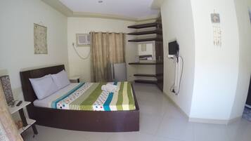Um quarto com cama, escrivaninha, televisão e guarda-roupa.