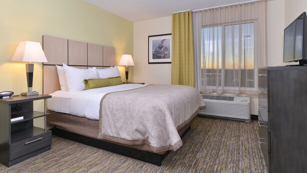 Quarto de hotel com cama, luminárias laterais, televisão de tela plana, aquecedor e janela com cortinas.