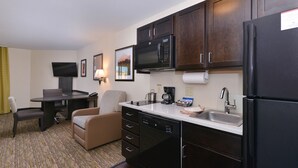 Uma cozinha de hotel compacta com micro-ondas, frigorífico, pia e um pequeno espaço de refeições com mesa e cadeiras.