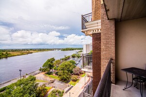 Uma varanda com vista para um rio, um estacionamento e um edifício de tijolos.