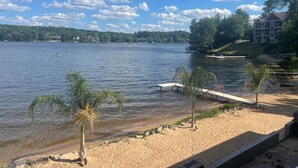 Vista para um lago com uma praia arenosa, um píer e uma fileira de árvores.