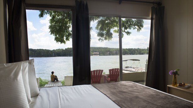 Quarto com cama grande, vista para um lago e uma cadeira junto à janela.